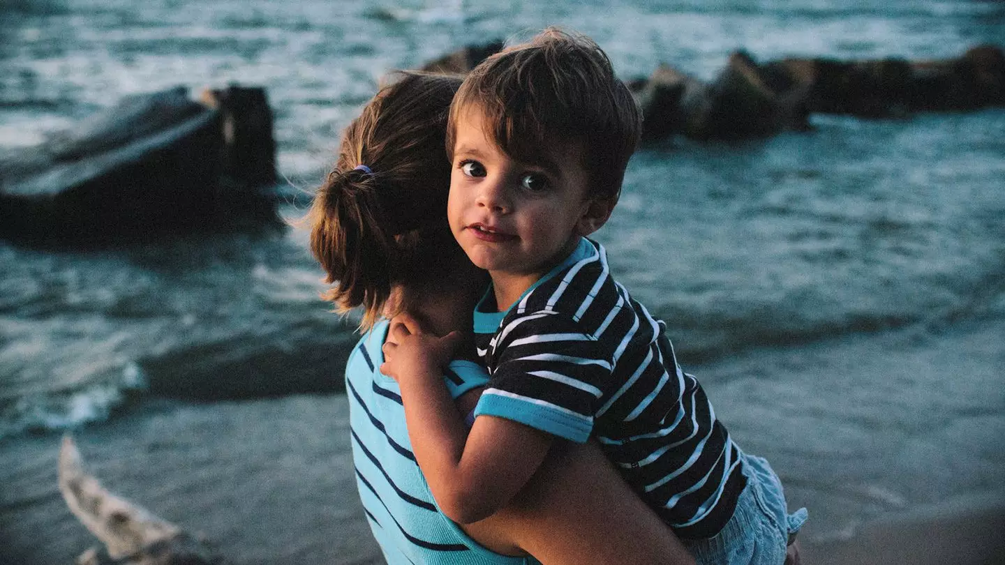 Anak nangkeup sosok indung nalika matahari terbenam di pantai