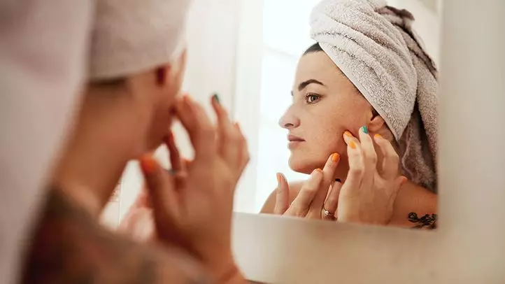 femme regardant l'acné de la peau dans le miroir