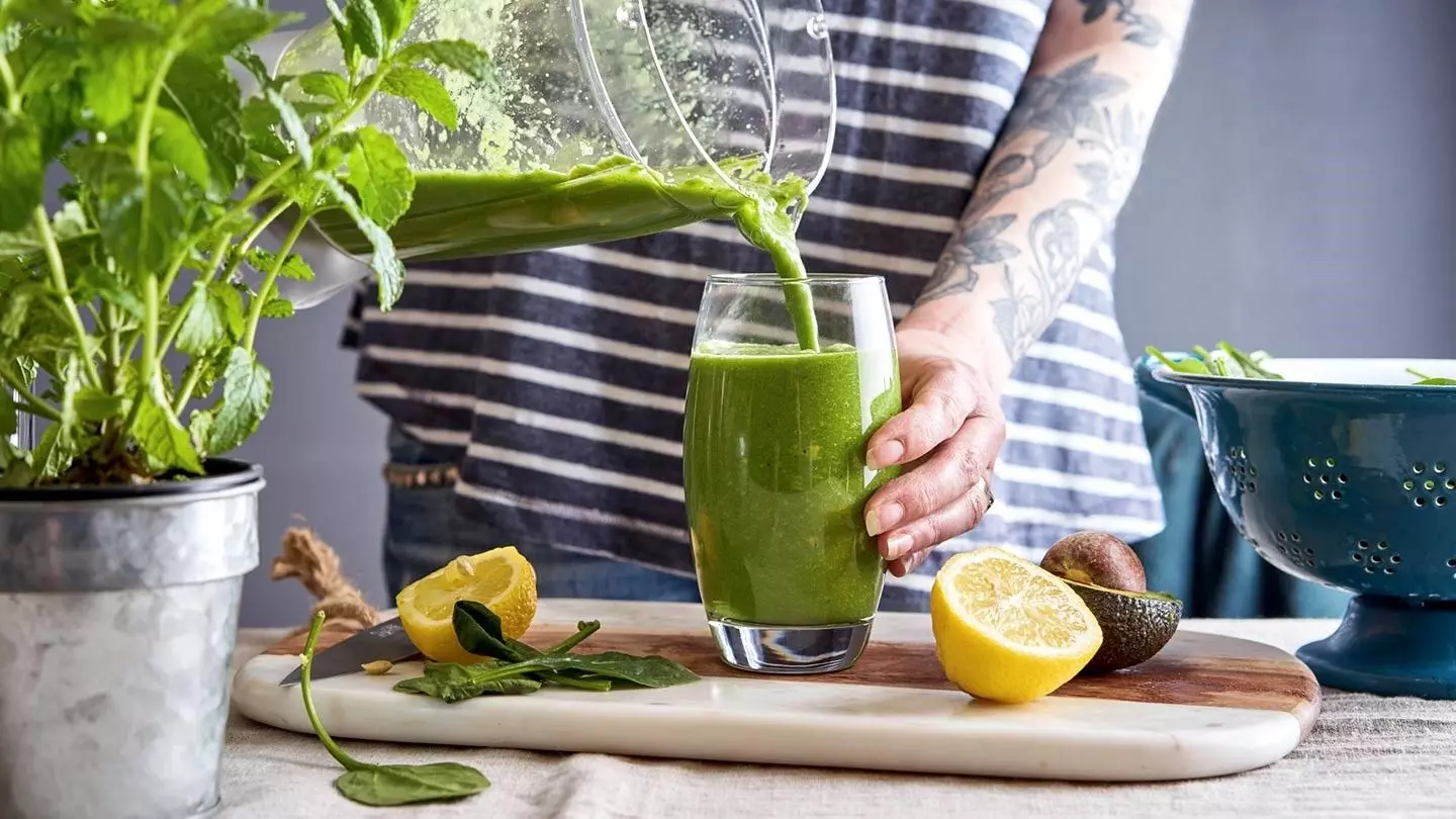 Persoa que bota un batido verde nun vaso.