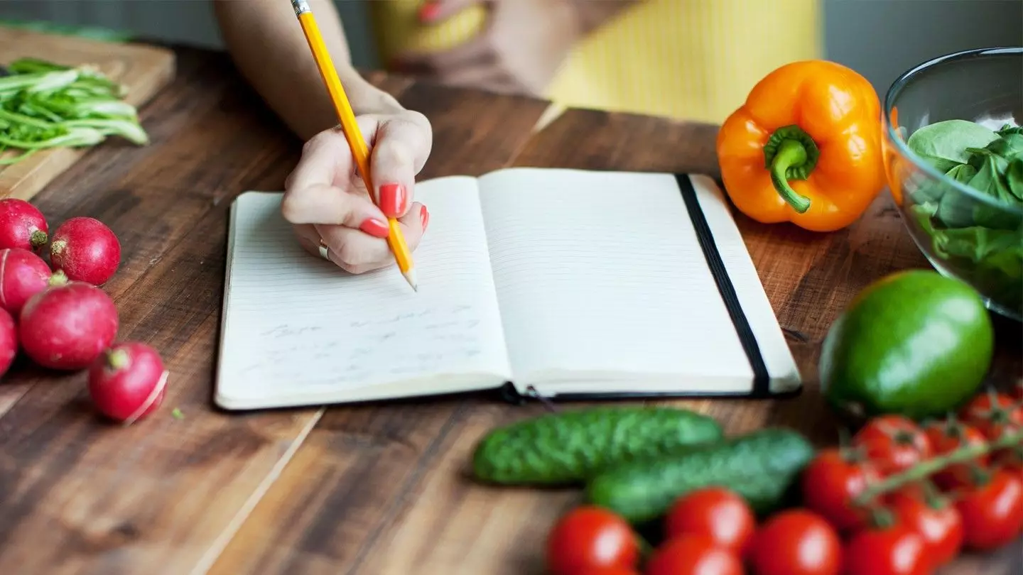 une femme écrivant dans un journal alimentaire entouré de légumes