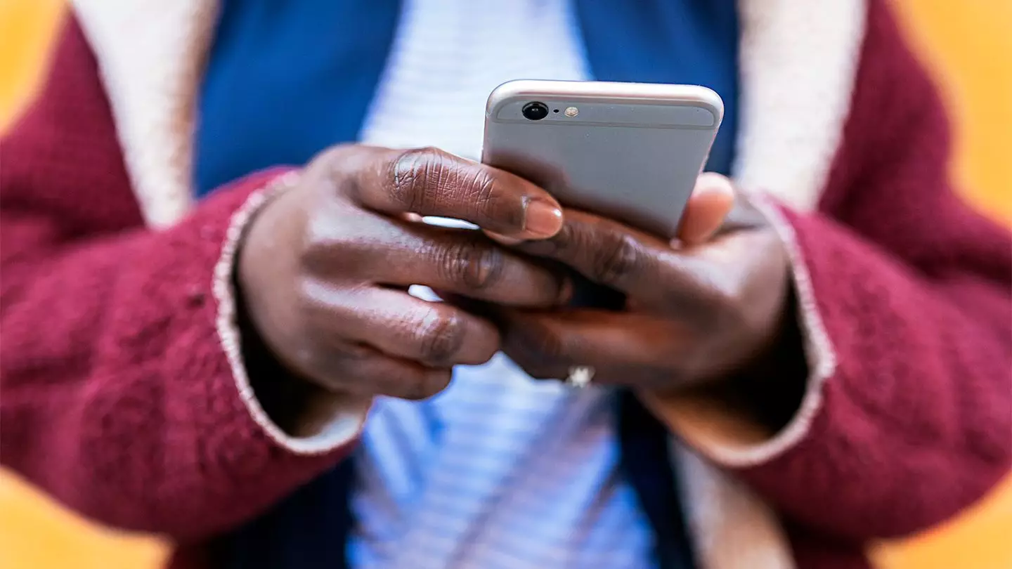 žena při pohledu na telefon v červené modré oblečení žluté pozadí