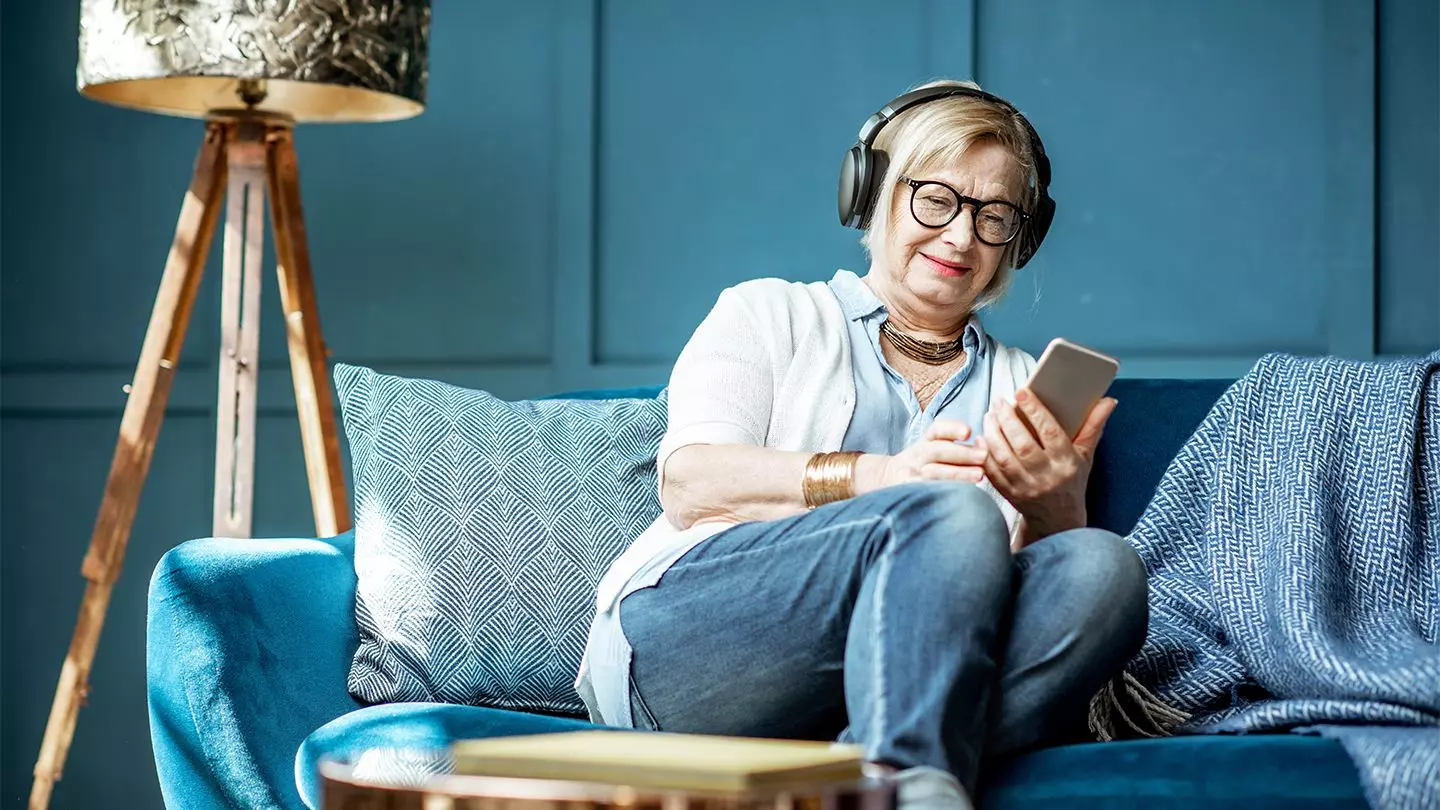 muller no sofá azul con auriculares escoitando o teléfono