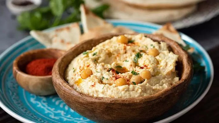 bát gỗ đầy hummus và đậu gà ngồi trên đĩa màu xanh