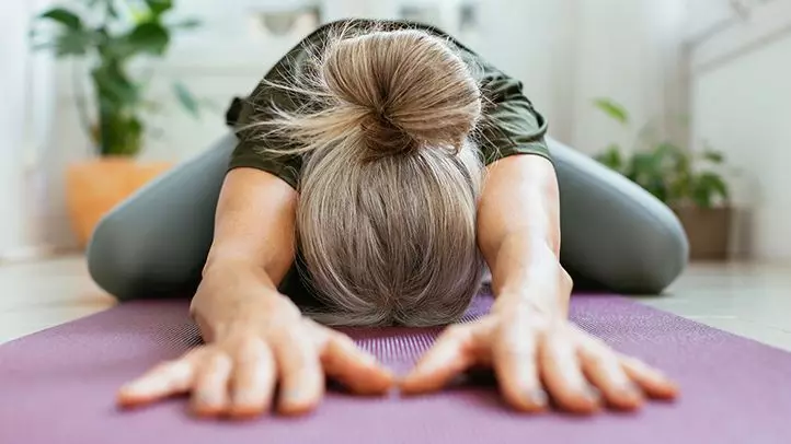 wanita senior berlatih yoga di atas tikar ungu